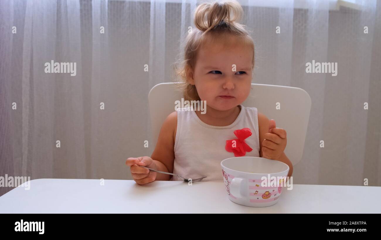 Infant girl eating baby food at a small childrens table on a white ...