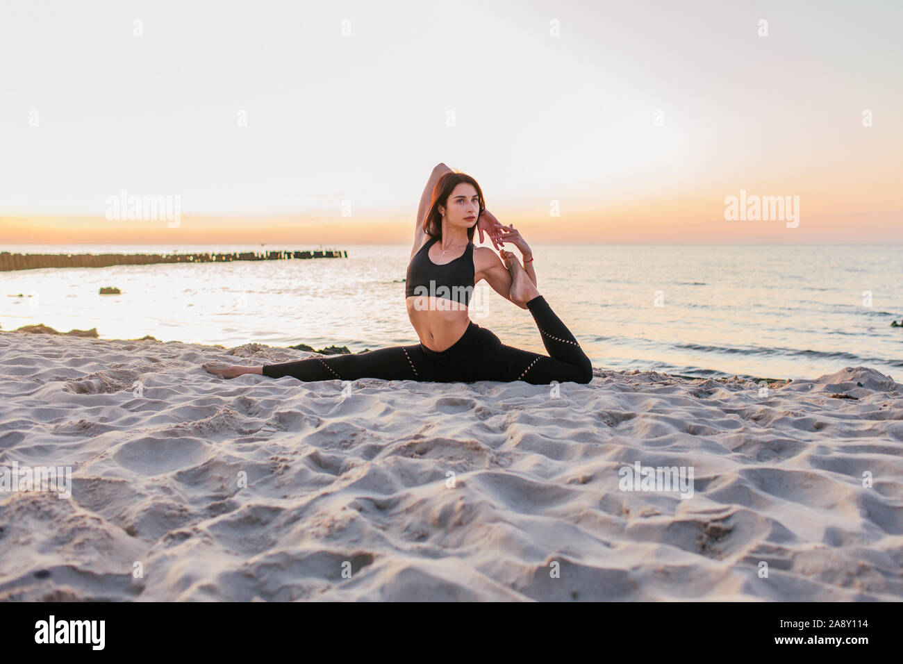 Slim strong young woman in black practicing yoga doing the splits on ...