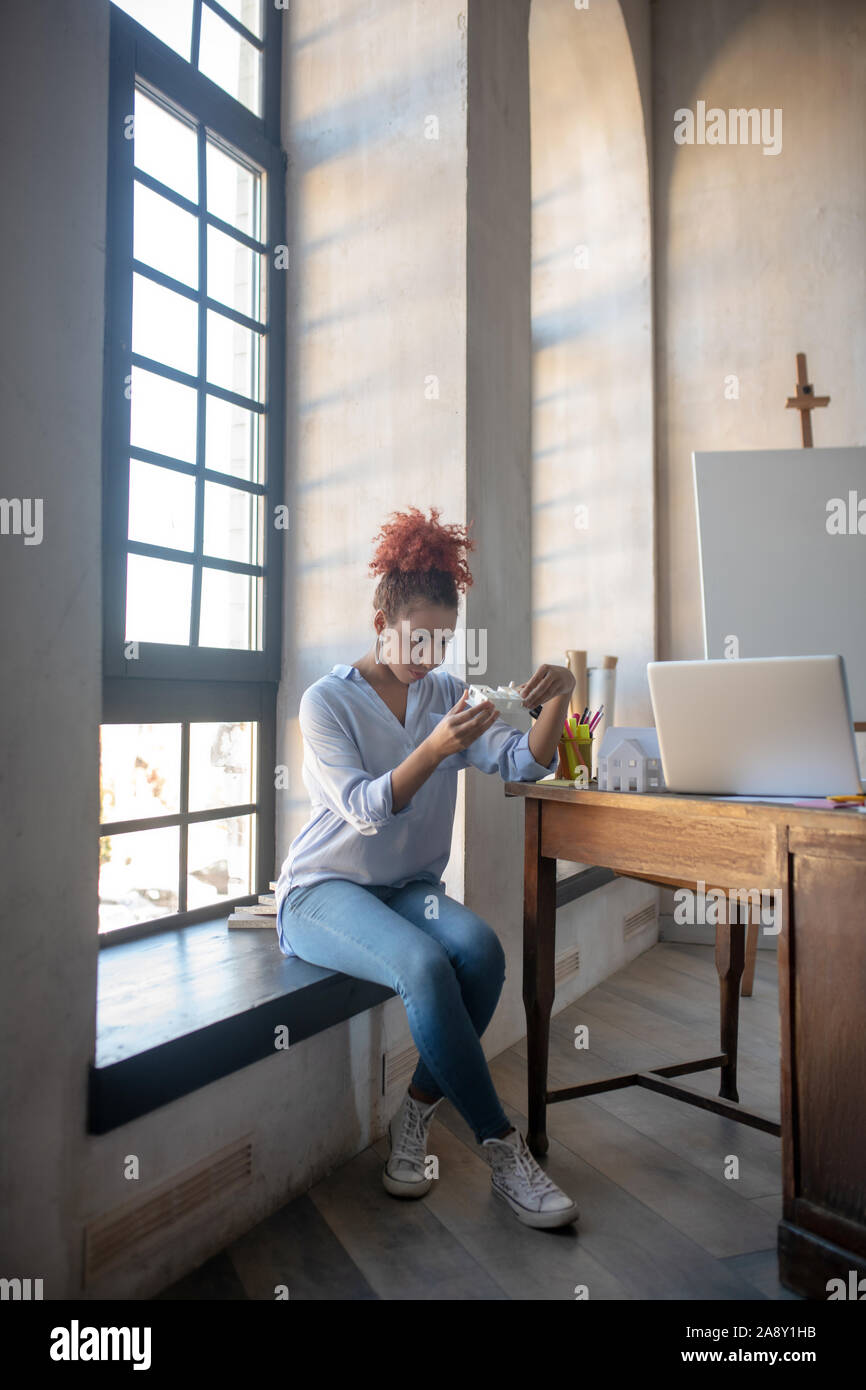Designer sitting on window sill and looking at house model Stock Photo ...