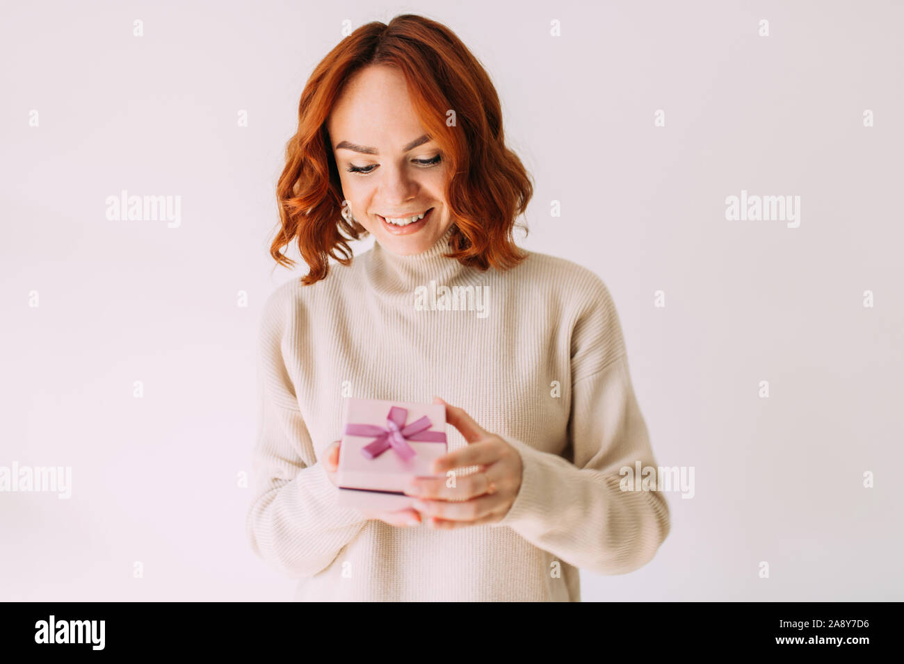Young birthday girl smiles, holding a pastel coloured gift box with ...