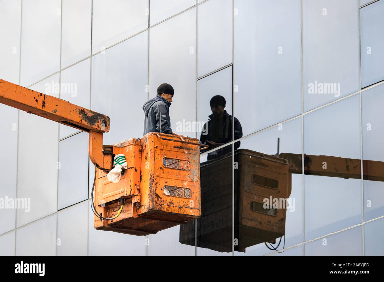 Male worker cleaning windows standing on a crane, outdoors in ...