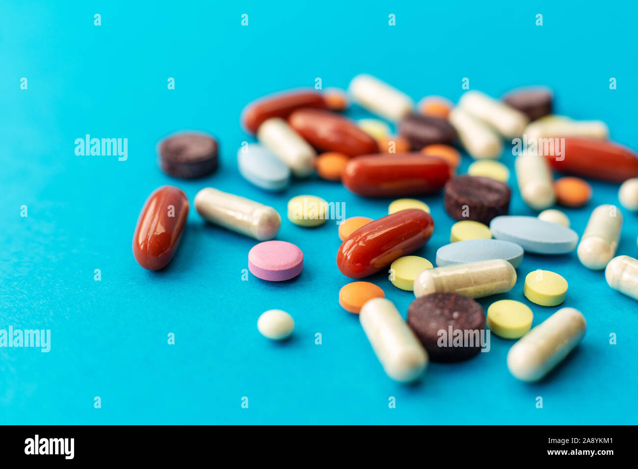A scattered handful of colored pills on a blue background. Medical ...