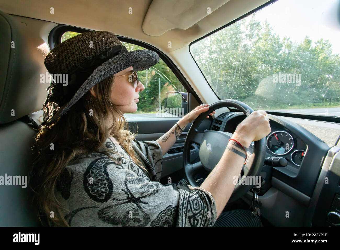 Young woman driving a SUV car with a big hat and heart shaped glasses ...
