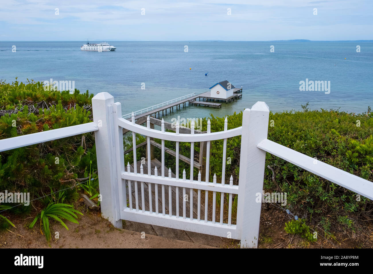 White wooden gate leading to pier with passenger ferry crossing the bay ...