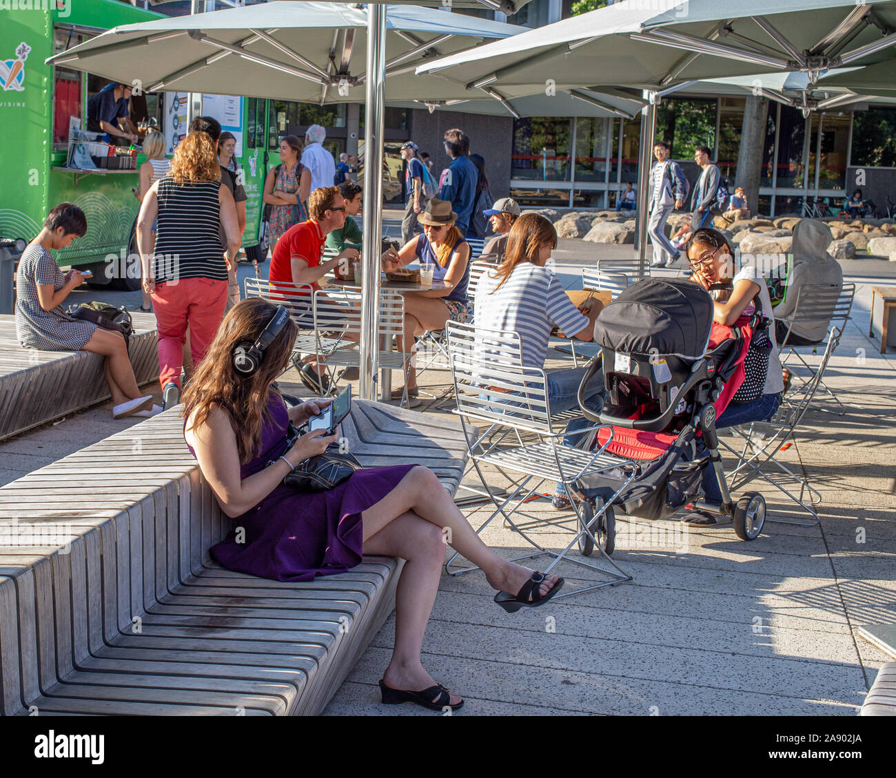 Students sitting outside at tables in Harvard Square, some using mobile ...