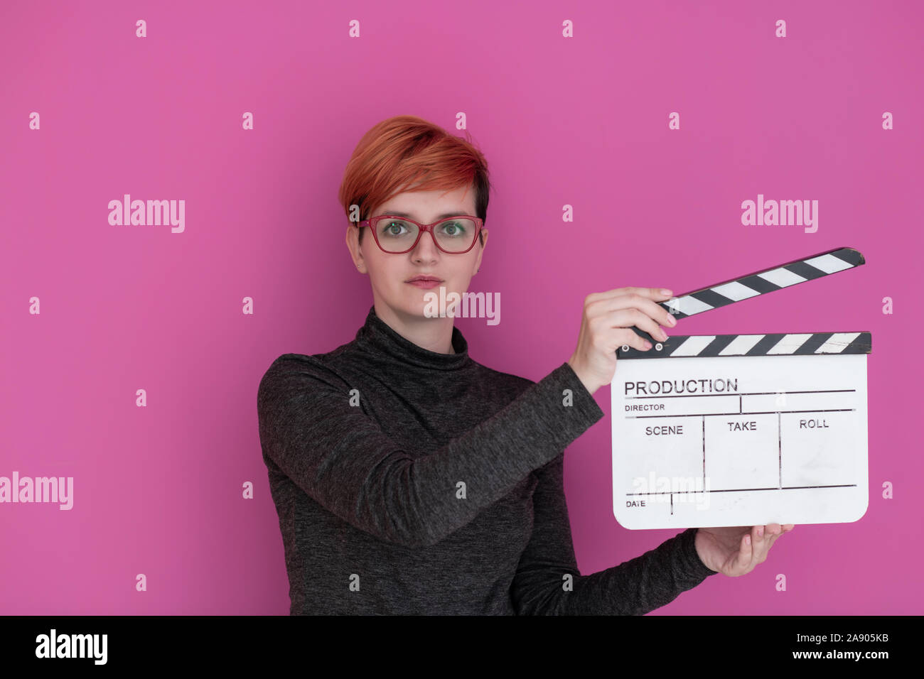 redhead woman holding movie clapper isolated against pink background ...