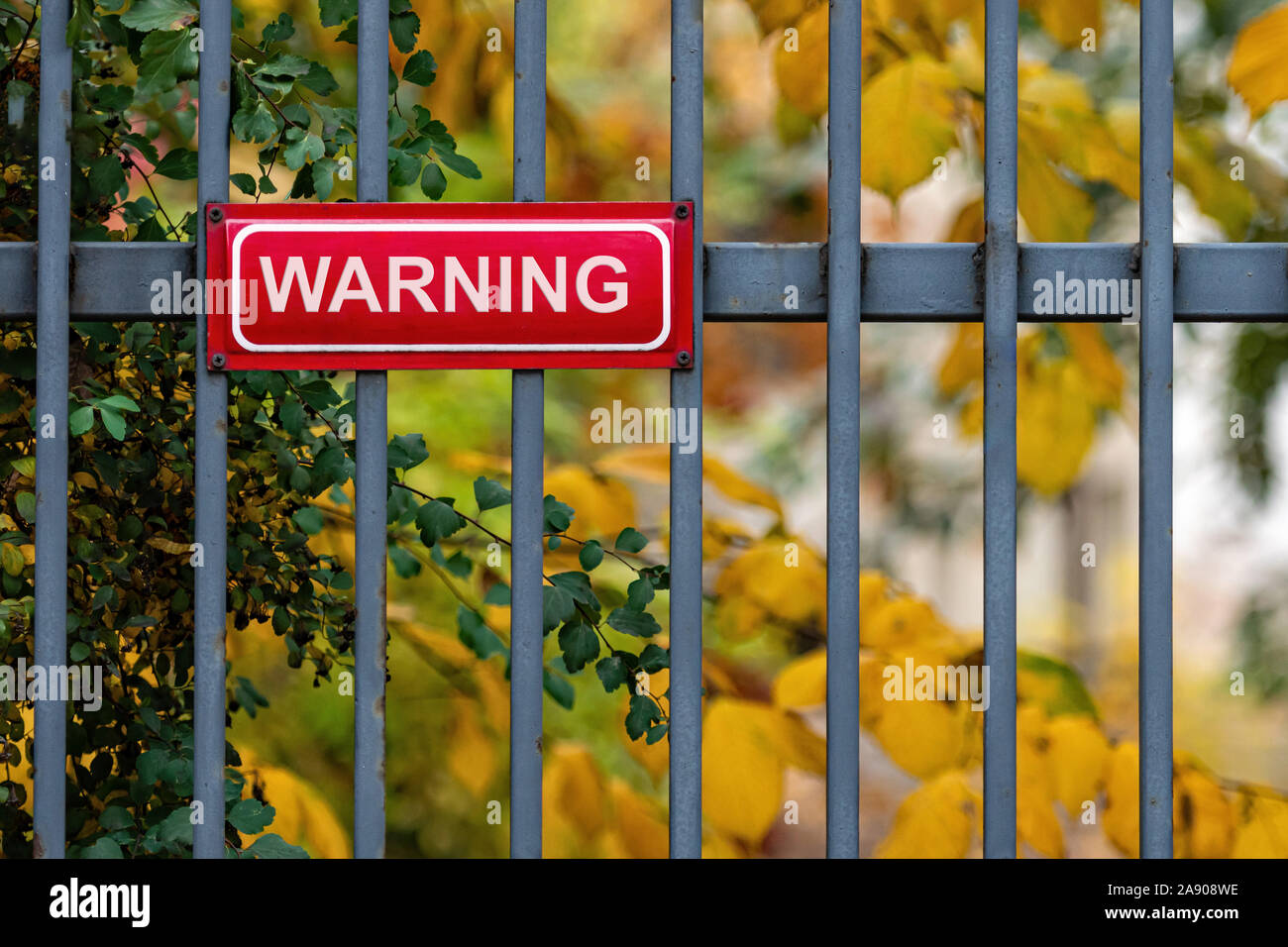 red metal sign with an inscription WARNING on a decorative metal fence ...