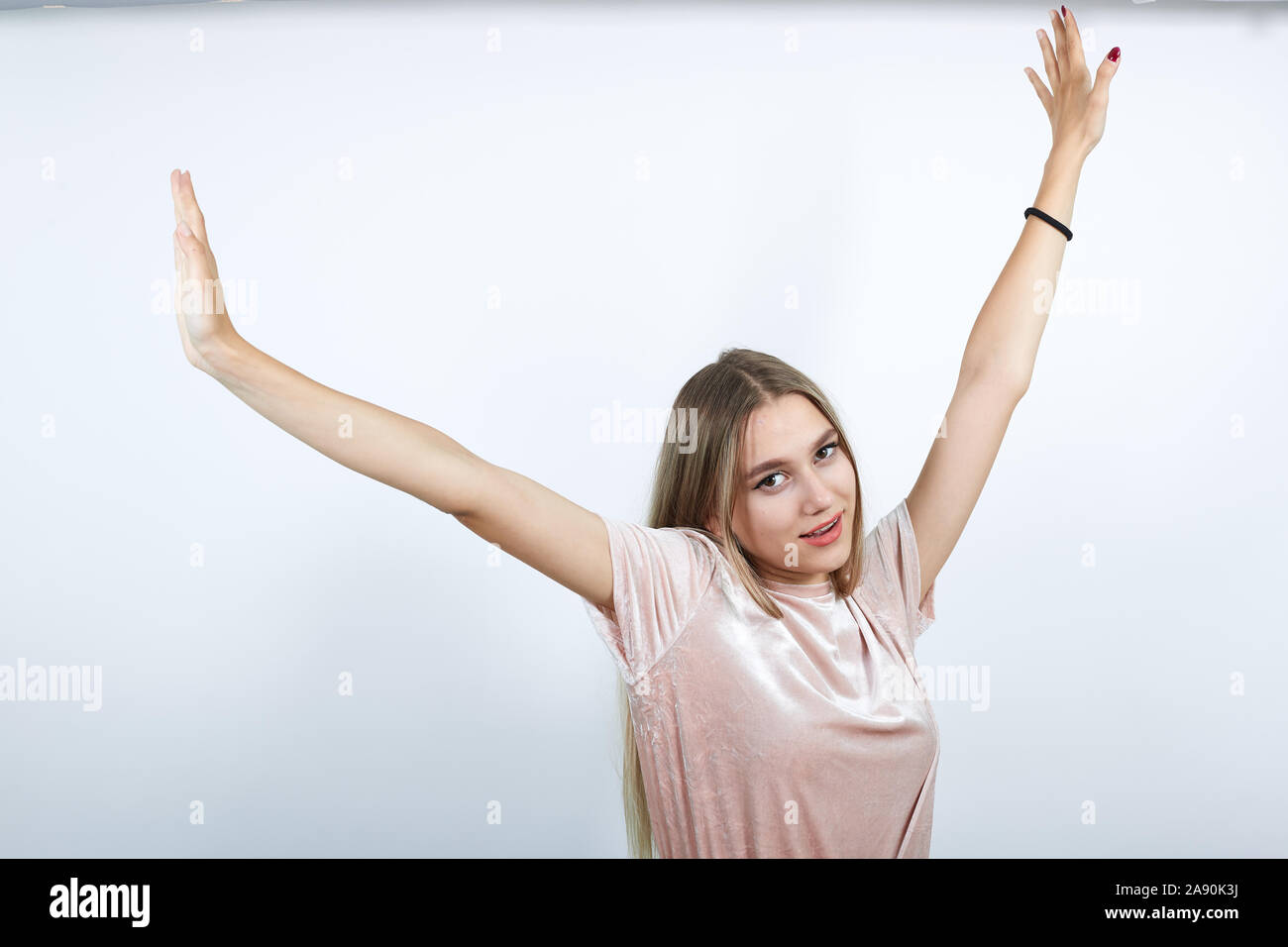 Smiling young woman in pastel shirt, looking directly, keeping hands up ...