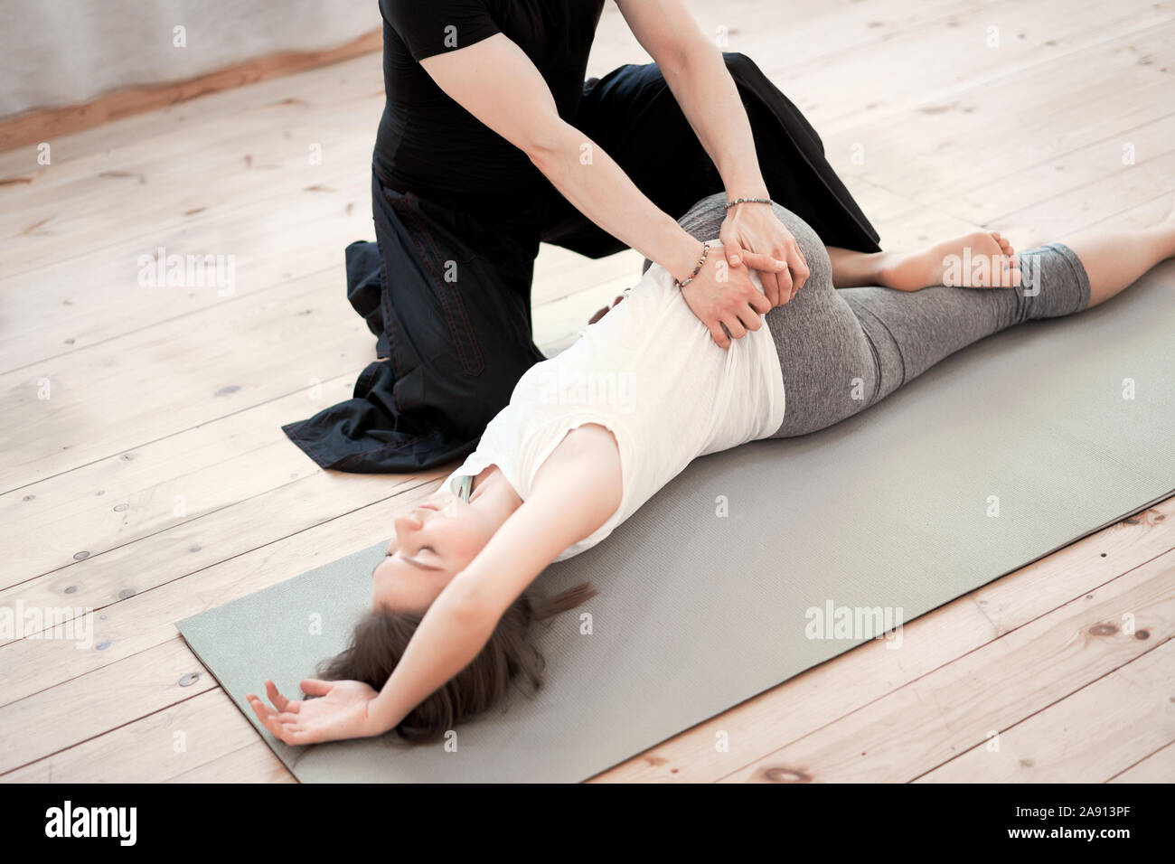 Sportswoman stretching on rug with male trainer in gym on wooden floor ...