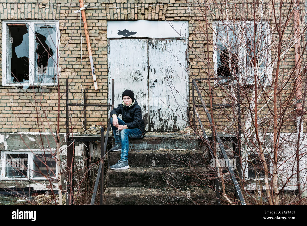 Teenage boy sitting at steps of abandoned building Stock Photo - Alamy