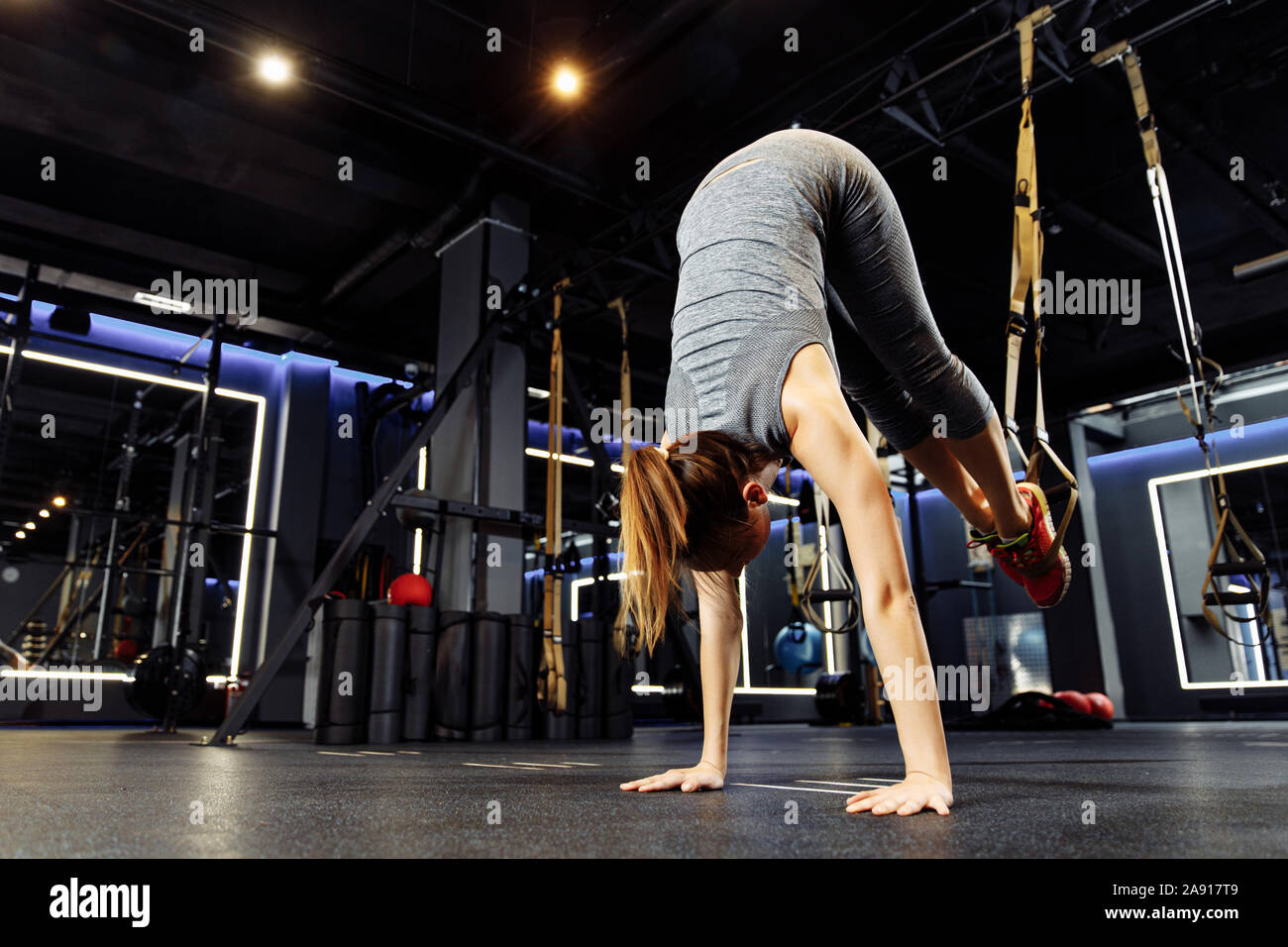 Athletic girl stretching with elastic bands in gym on dark background ...