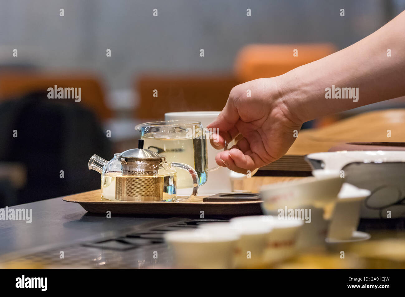 Barista male hands placing a glass teapot with tea in strands on a tray ...