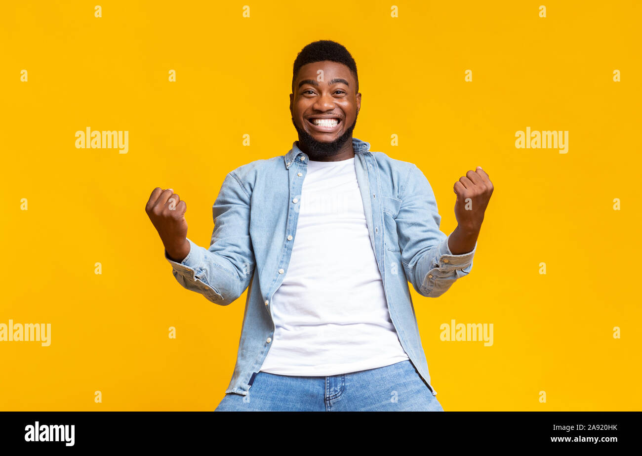 Portrait of overjoyed black man celebrating success with clenched fists ...