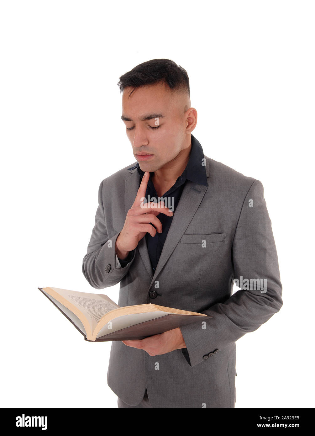 A young handsome east Indian man standing in a gray suit with a book in ...