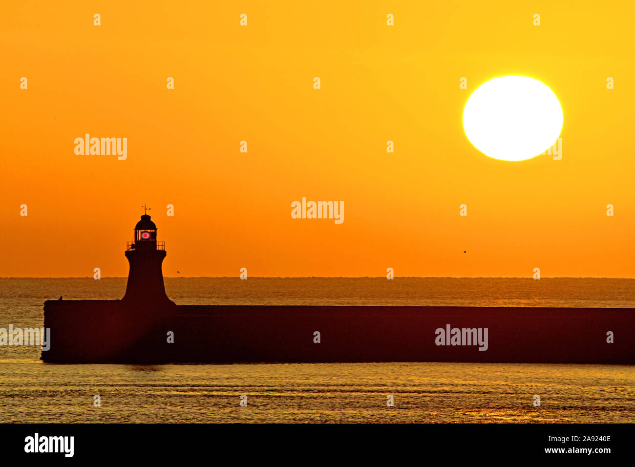 Large orange sun at sunrise and lighthouse with pier Stock Photo - Alamy