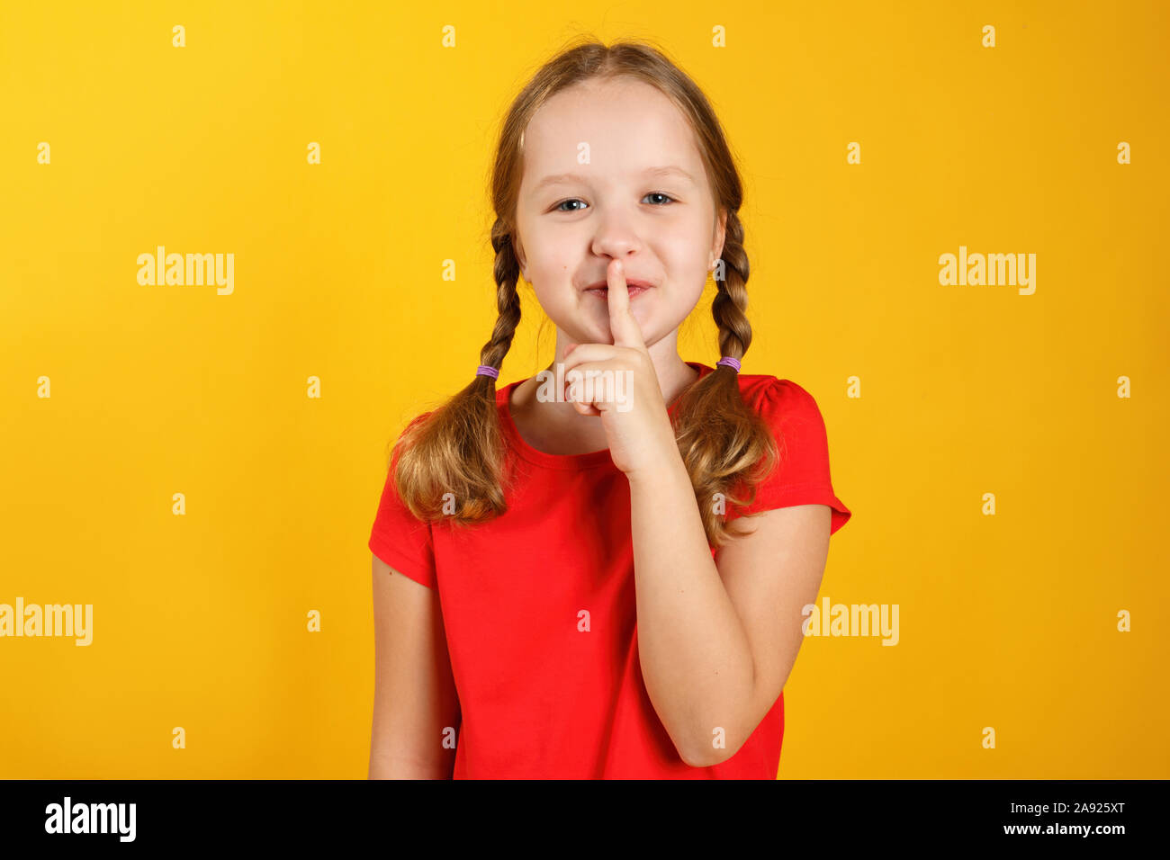 Child showing shh sign on a yellow background. Portrait of a cute ...