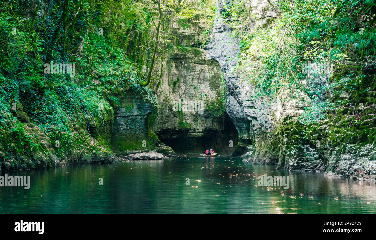 mountain river with tall cliffs and green plants and tourists in a boat ...