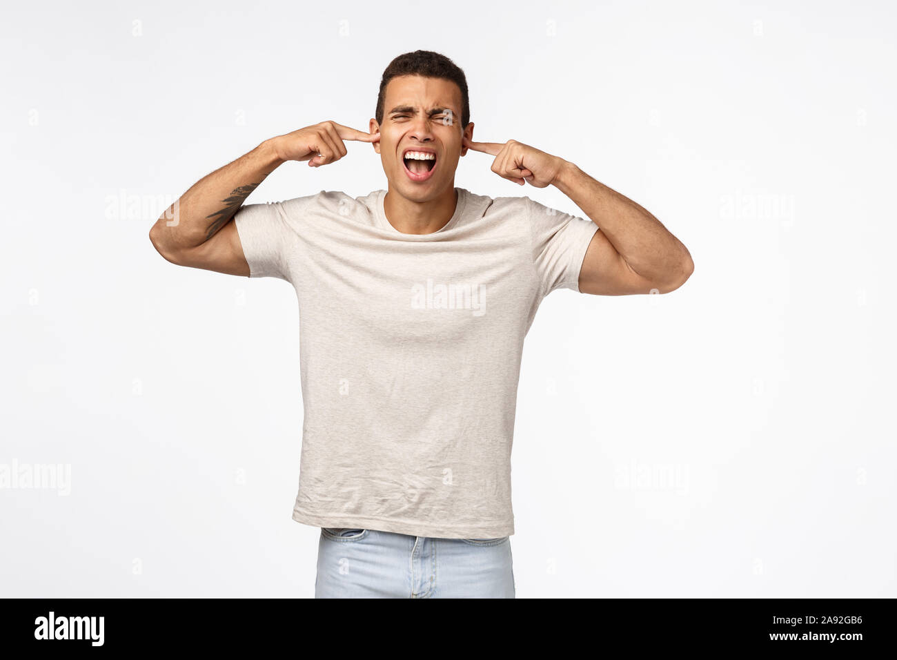 Angry and annoyed athletic young man close ears with fingers, yelling ...