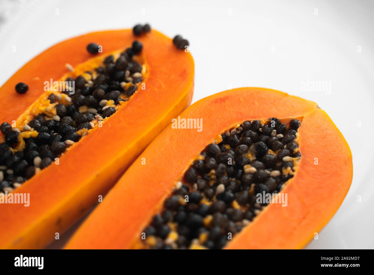 Half cut ripe papaya with seed on a white plate. Slices of sweet papaya ...