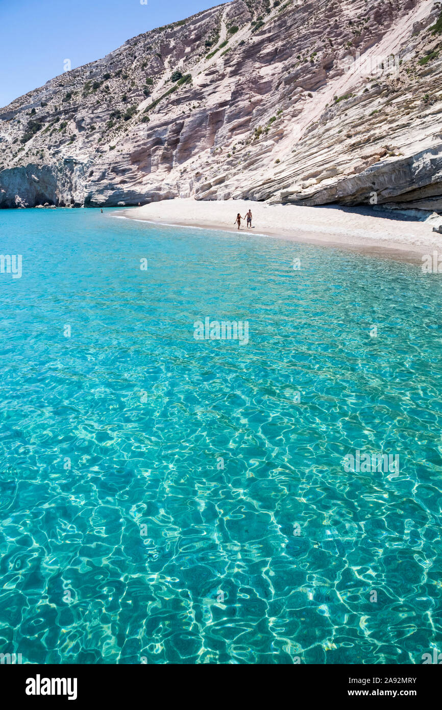 Tourists walking on the beach along the clear, turquoise water of ...