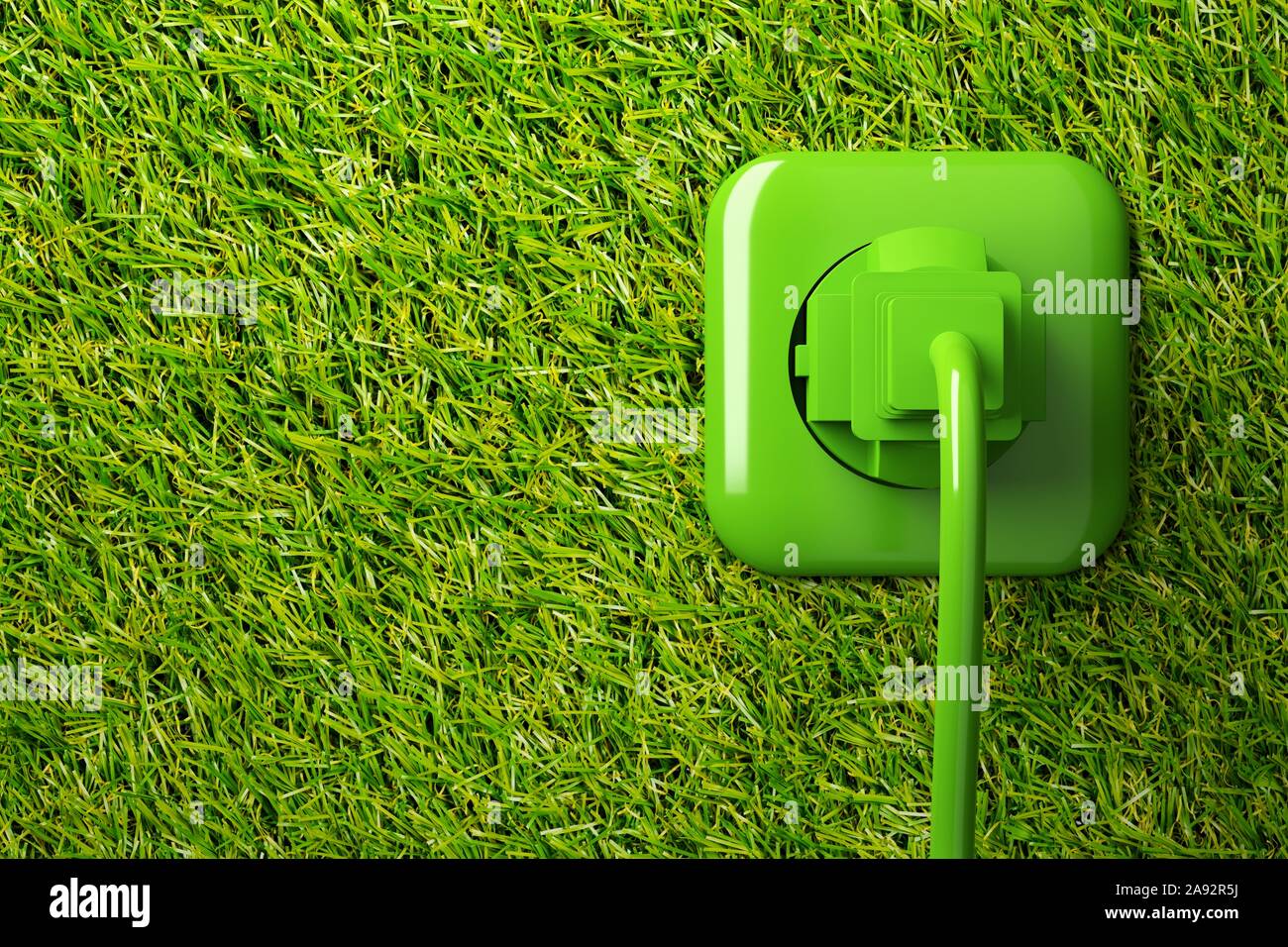 Green power cord in wall socket on grass background with copy space ...