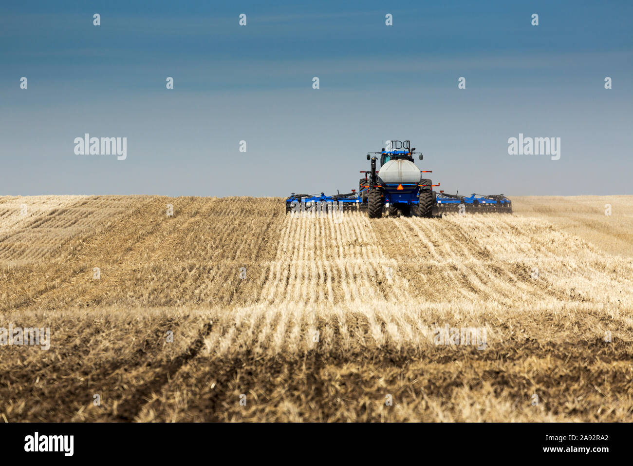 Back view of air seeder, seeding a stubble field with blue sky and hazy ...