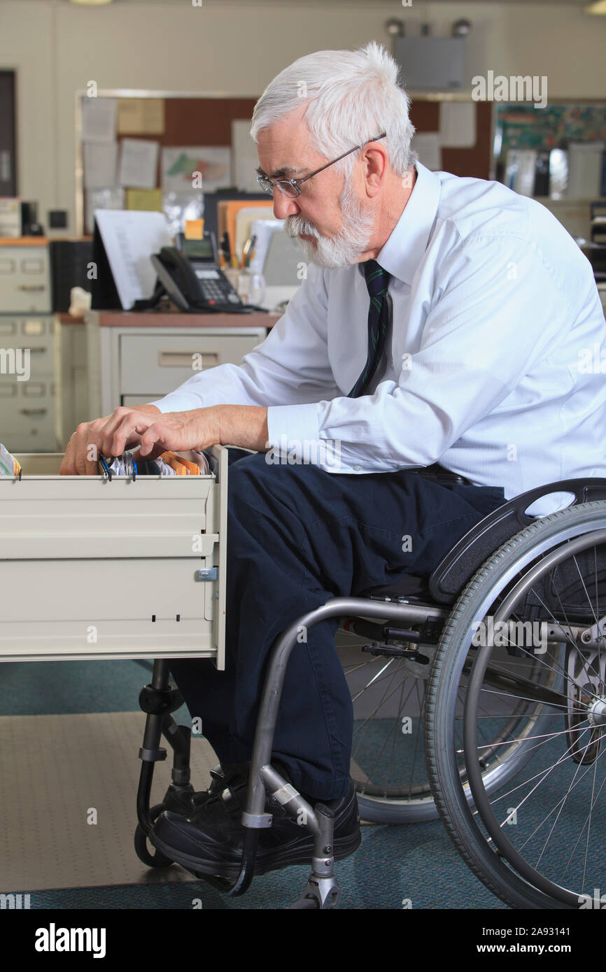 Man with Muscular Dystrophy in a wheelchair filing papers in his office ...