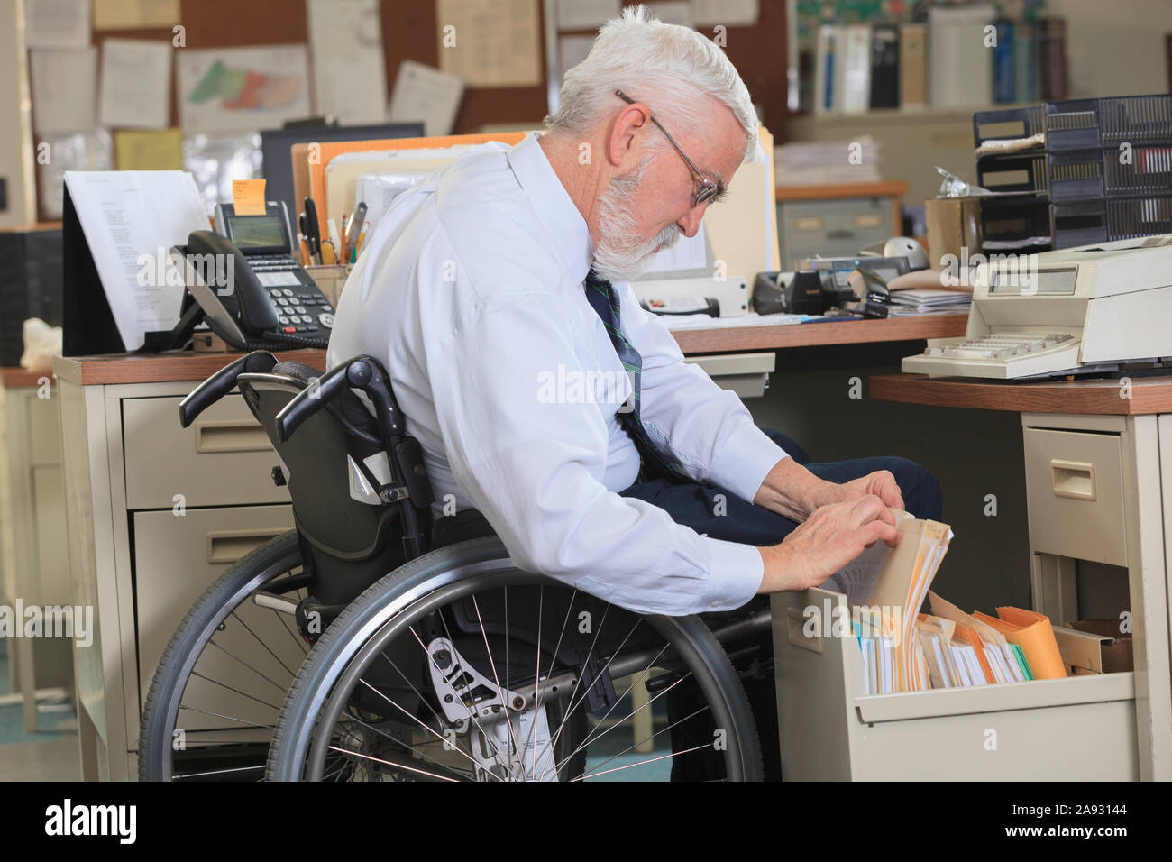 Man with Muscular Dystrophy in a wheelchair looking up paperwork in his ...
