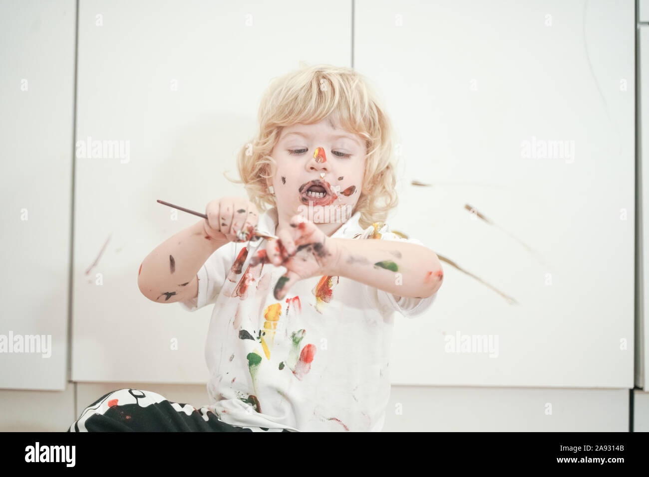 two year old boy with hands and face painted in colorful paints ready ...