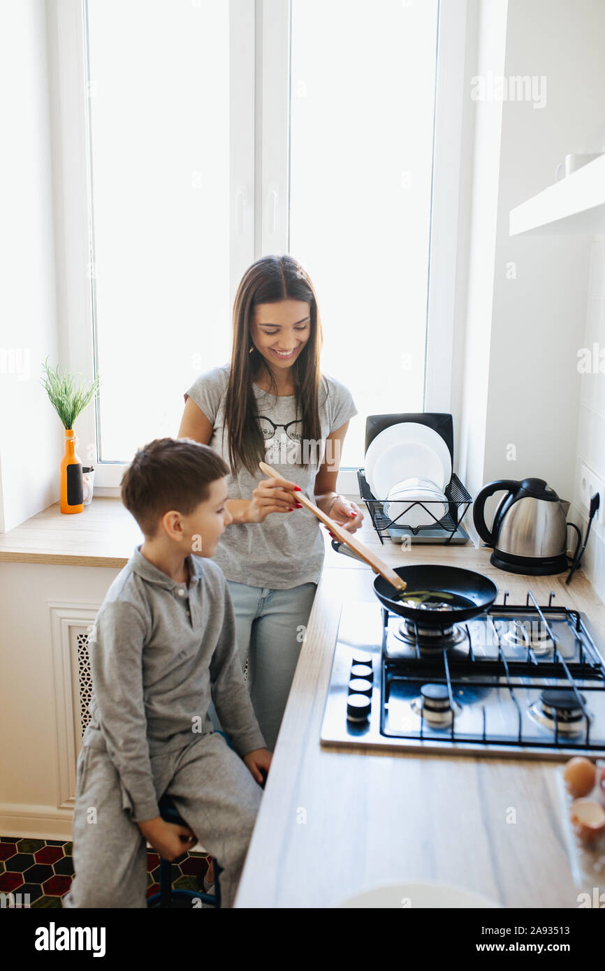 Cute little boy and his mom smiling and cooking in kitchen at home ...