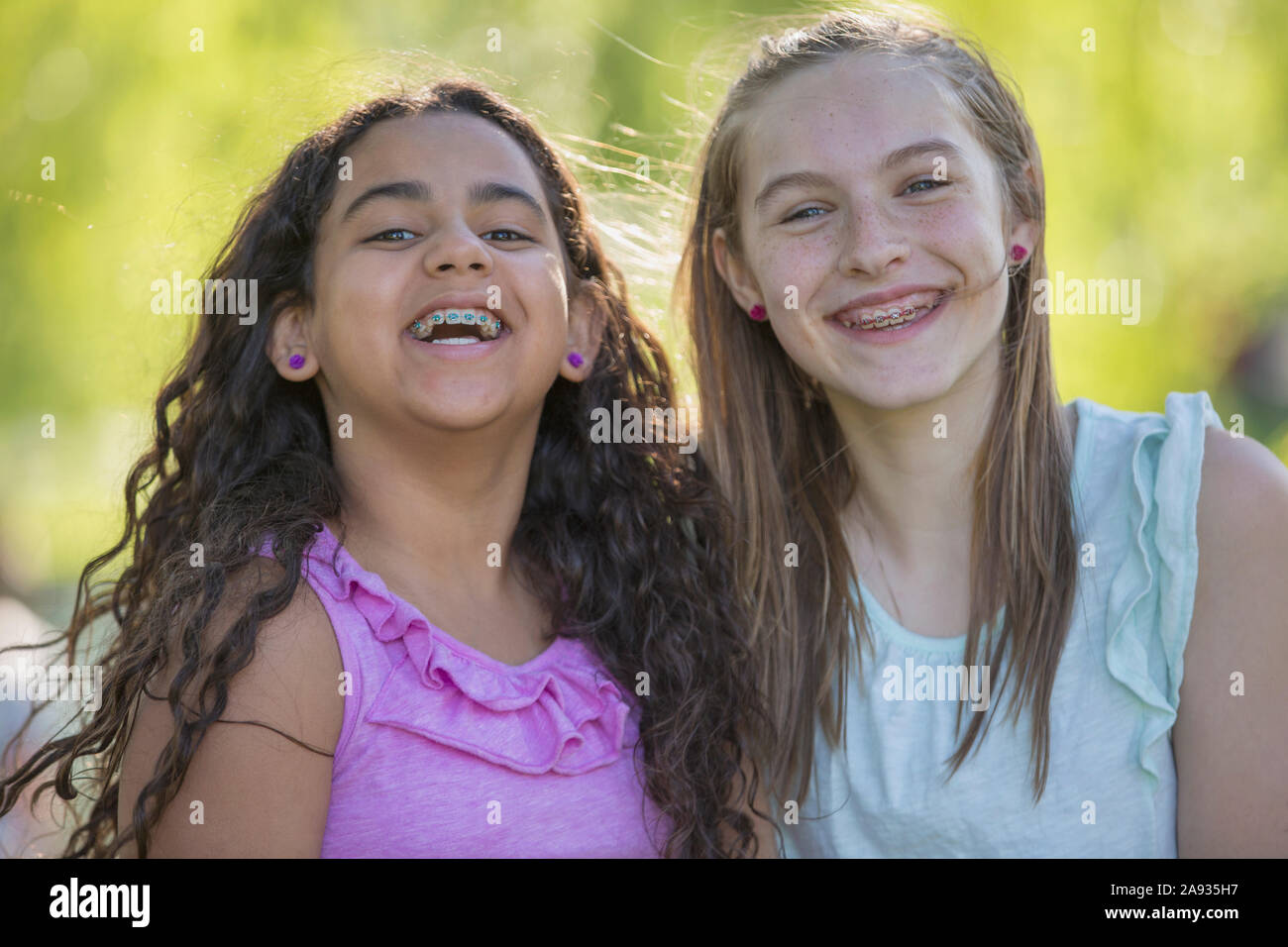 Portrait of two Hispanic teen sisters smiling with braces in a park ...