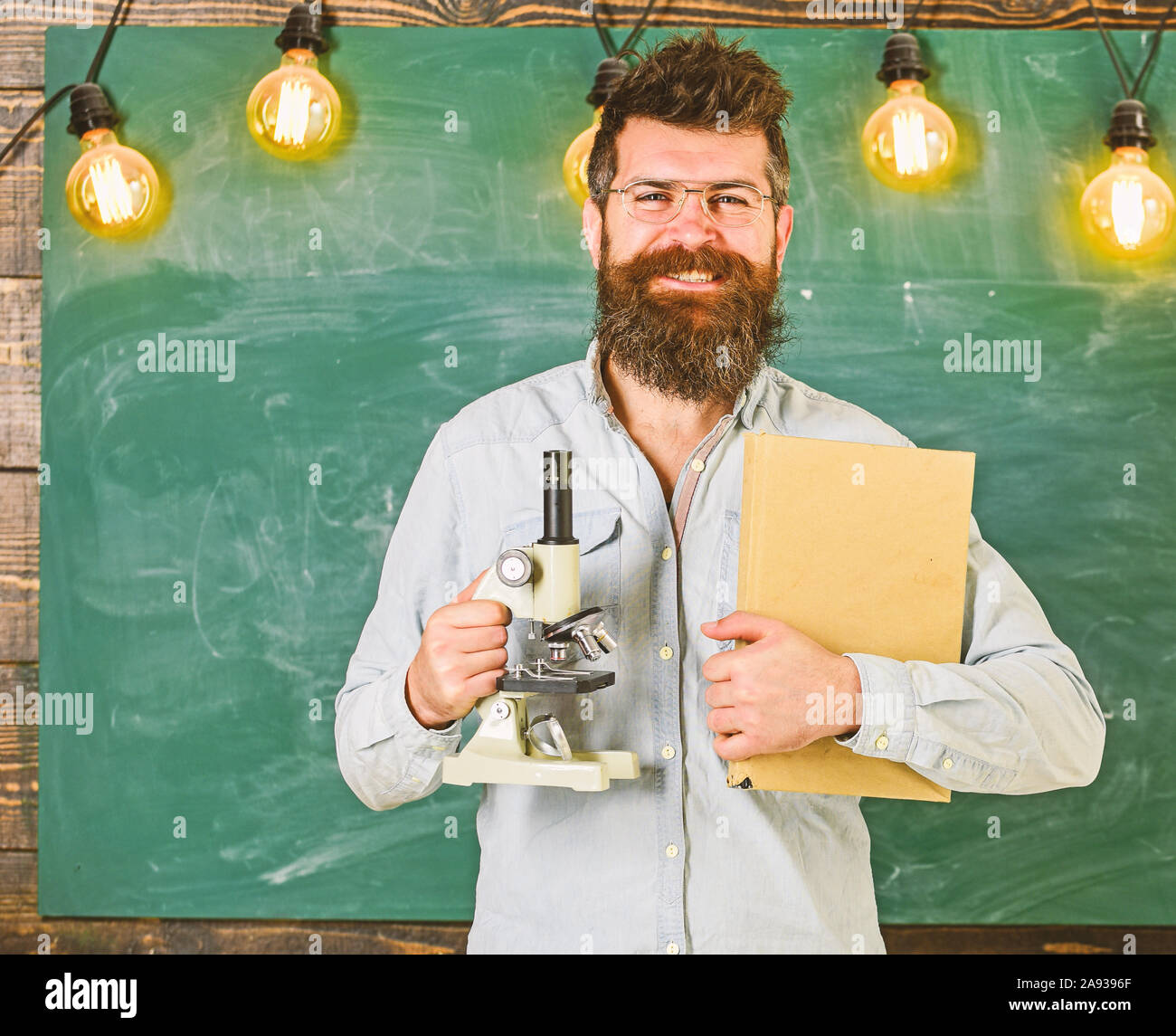 Teacher in eyeglasses holds book and microscope. Science concept. Man ...