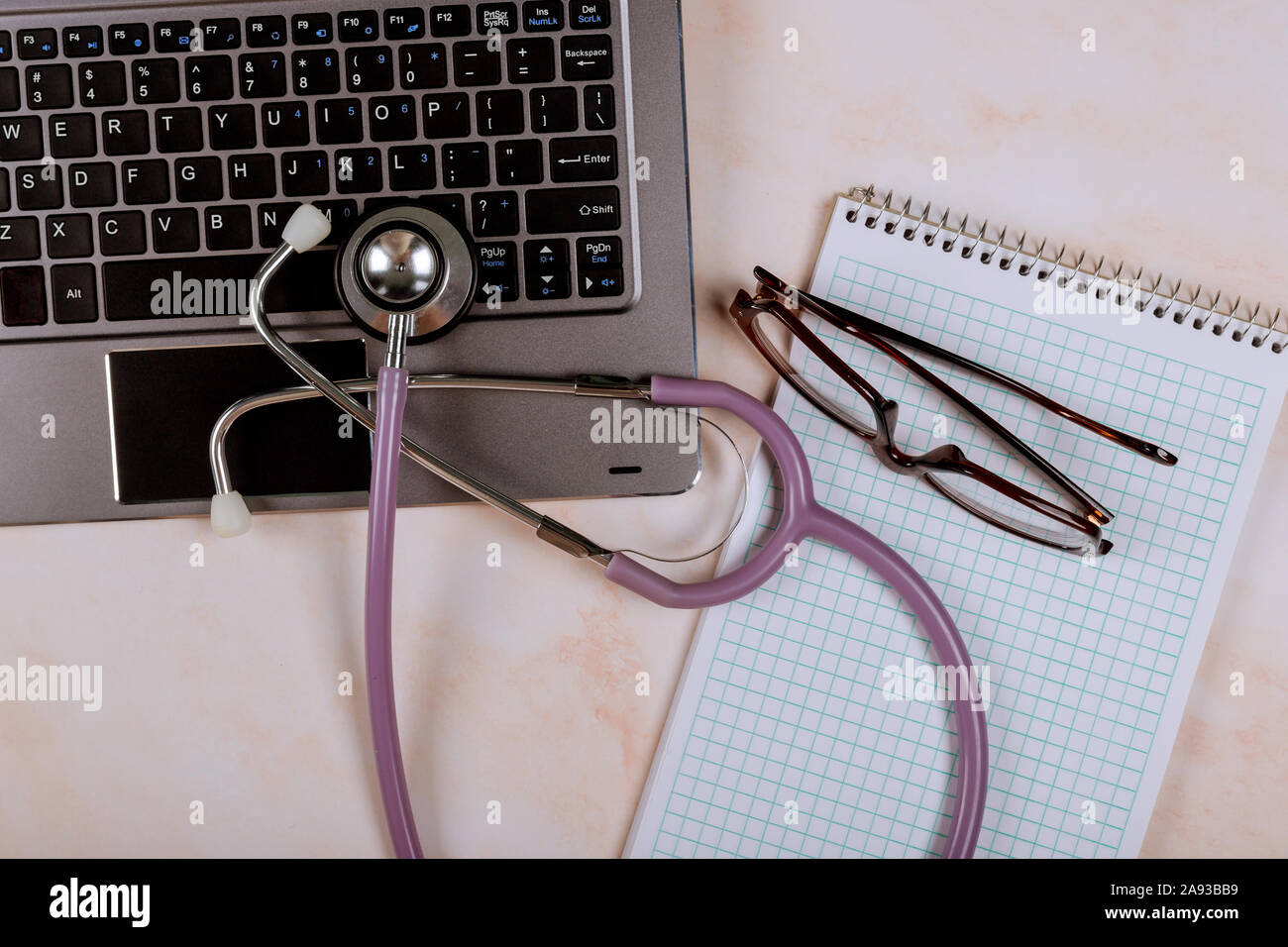 Medical stethoscope on laptop computer keyboard with blank notebook and ...