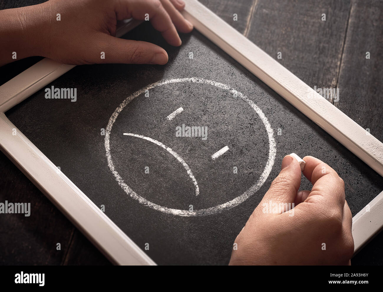 Hand drawing sad smiley face on black chalk board. Negative human ...