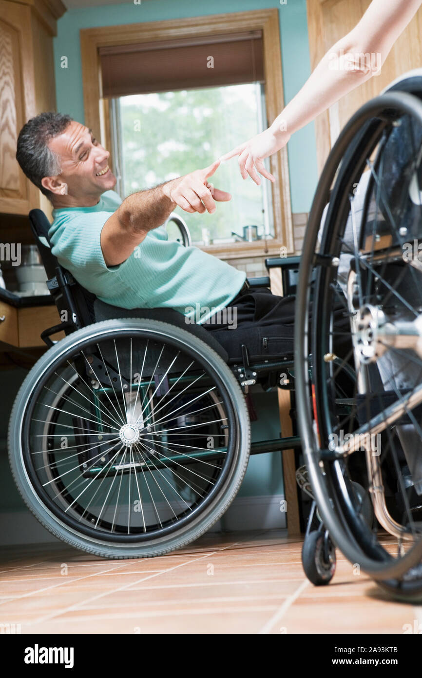 Mid adult man sitting in a wheelchair and reaching out for the finger ...