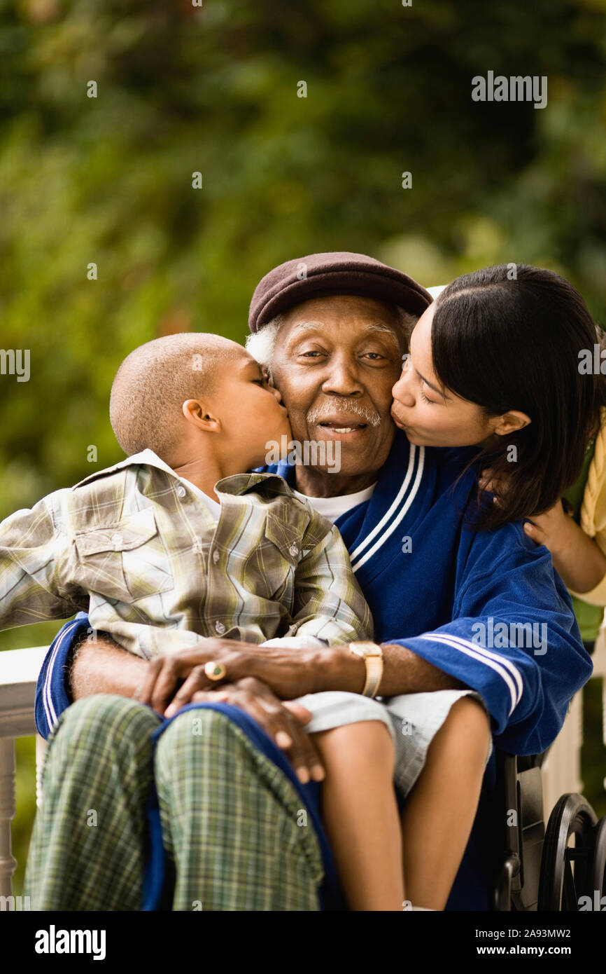 Senior Man Sitting In Wheelchair Is Kissed On The Cheek By His Grandson