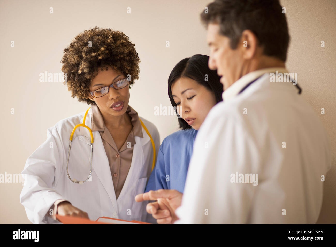 Three doctors discussing patient files in a corridor Stock Photo - Alamy