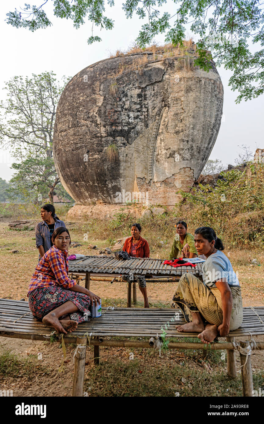 Local villagers sitting at a table near (Chinthe) the Lions of Stone ...
