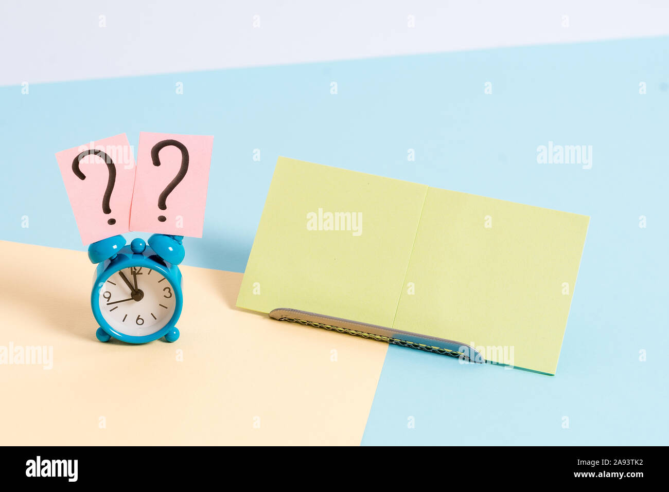 Mini size alarm clock beside a Paper sheet placed tilted on pastel ...