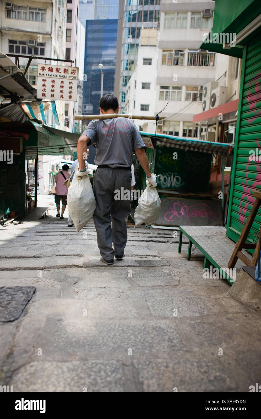 Man carrying two sacks attached to a piece of wood lying across his ...