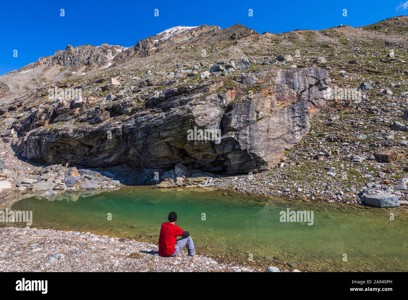 A hiker relaxes beside a pool of water in the Alaska Range; Alaska ...
