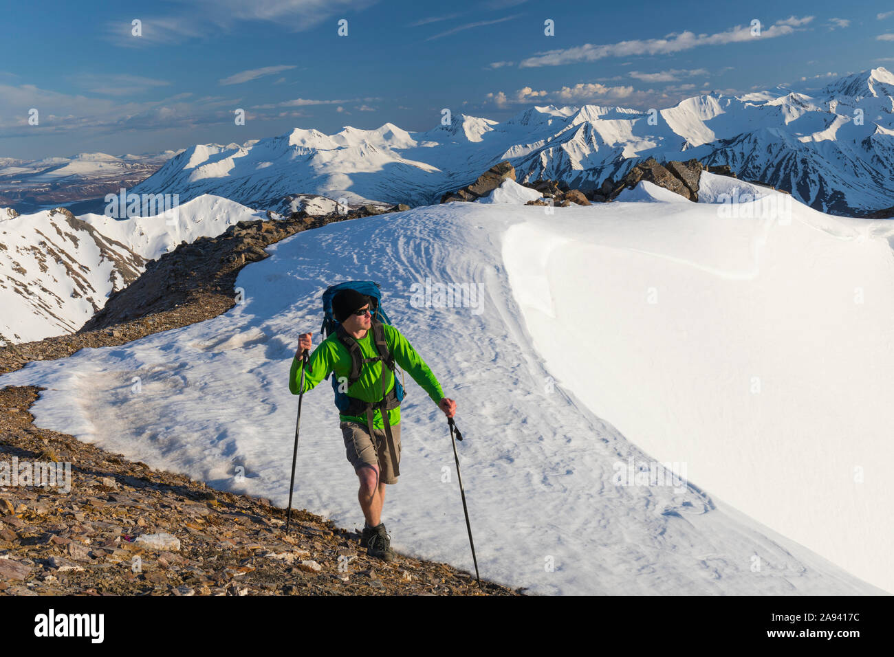 A hiker traverses a snowy ridge in the Alaska Range in early summer ...
