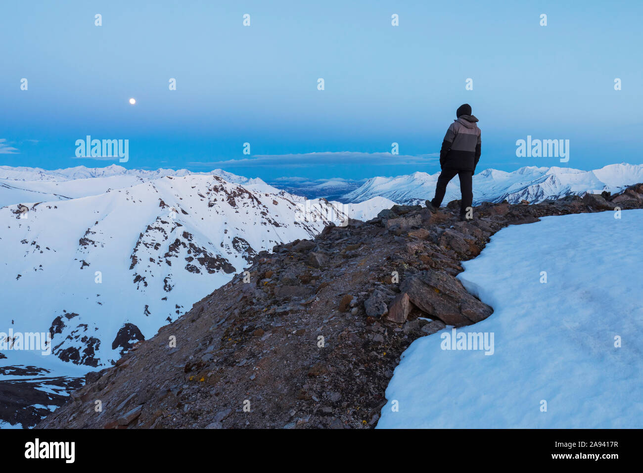 A hiker on a ridge in the Alaska Range looks toward the moon over a ...