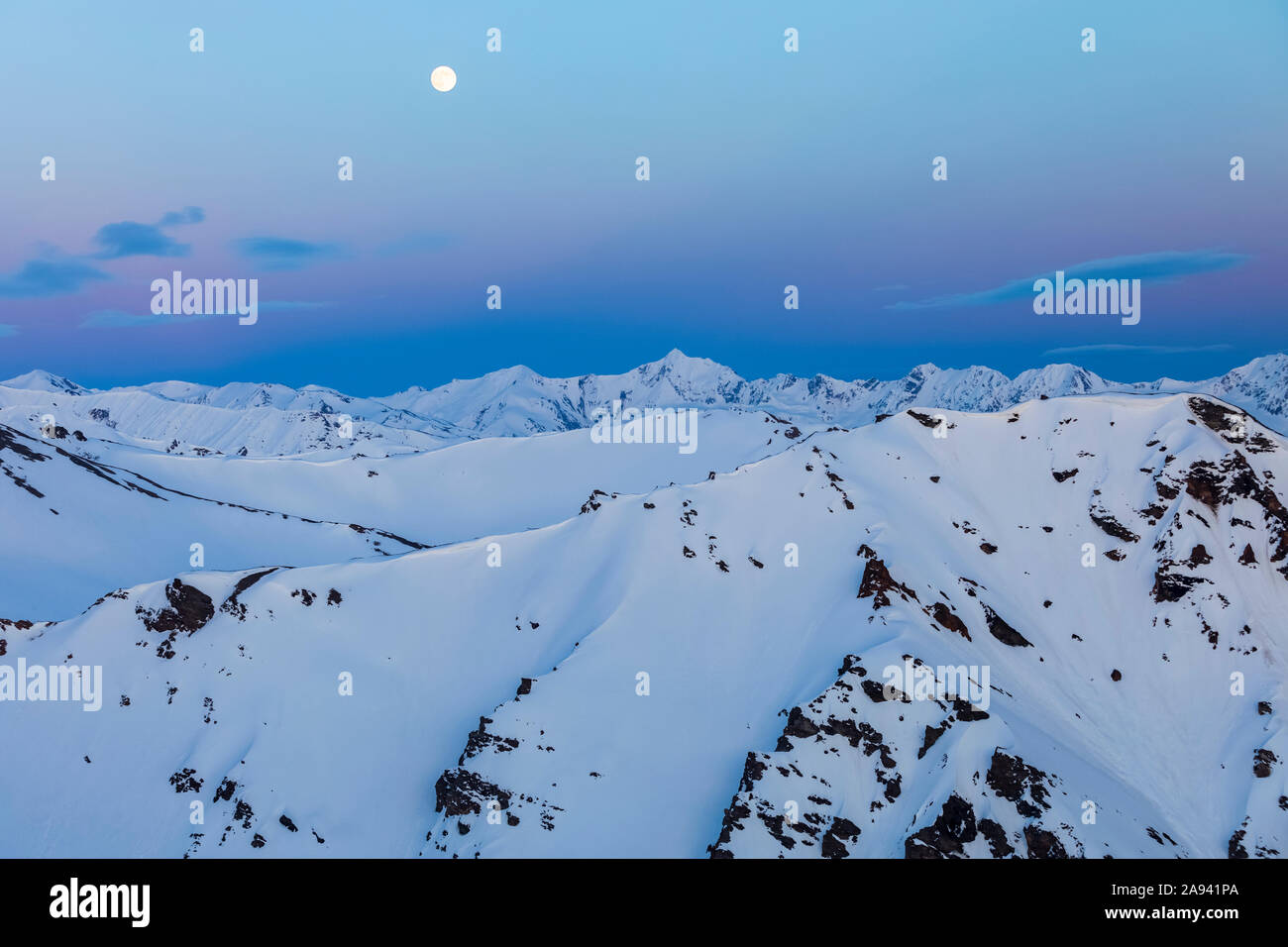 The moon rises over snowy mountain ridges after sunset in the Alaska ...