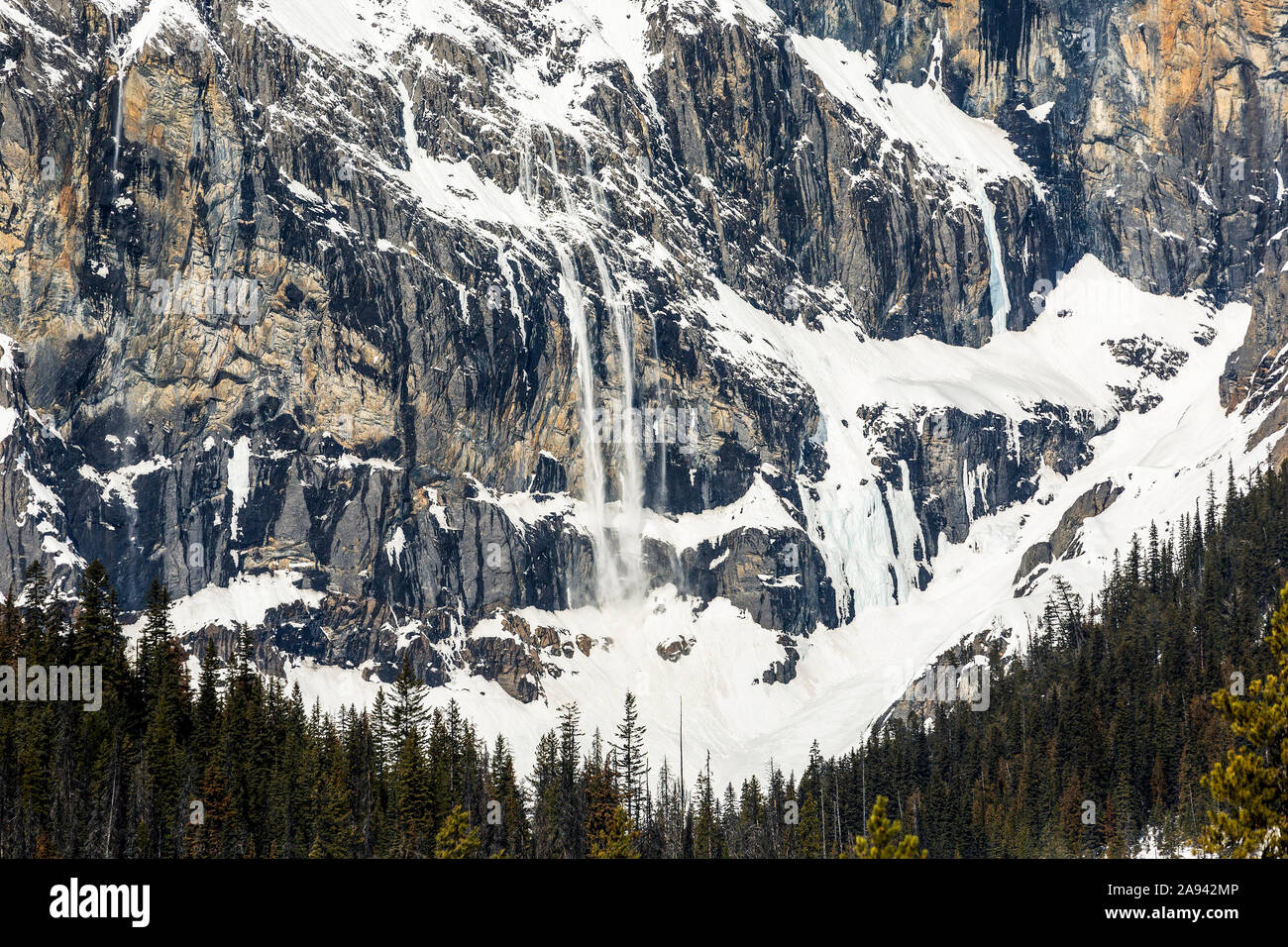 Close-up of mountain cliff face with avalanche snow cascading over ...