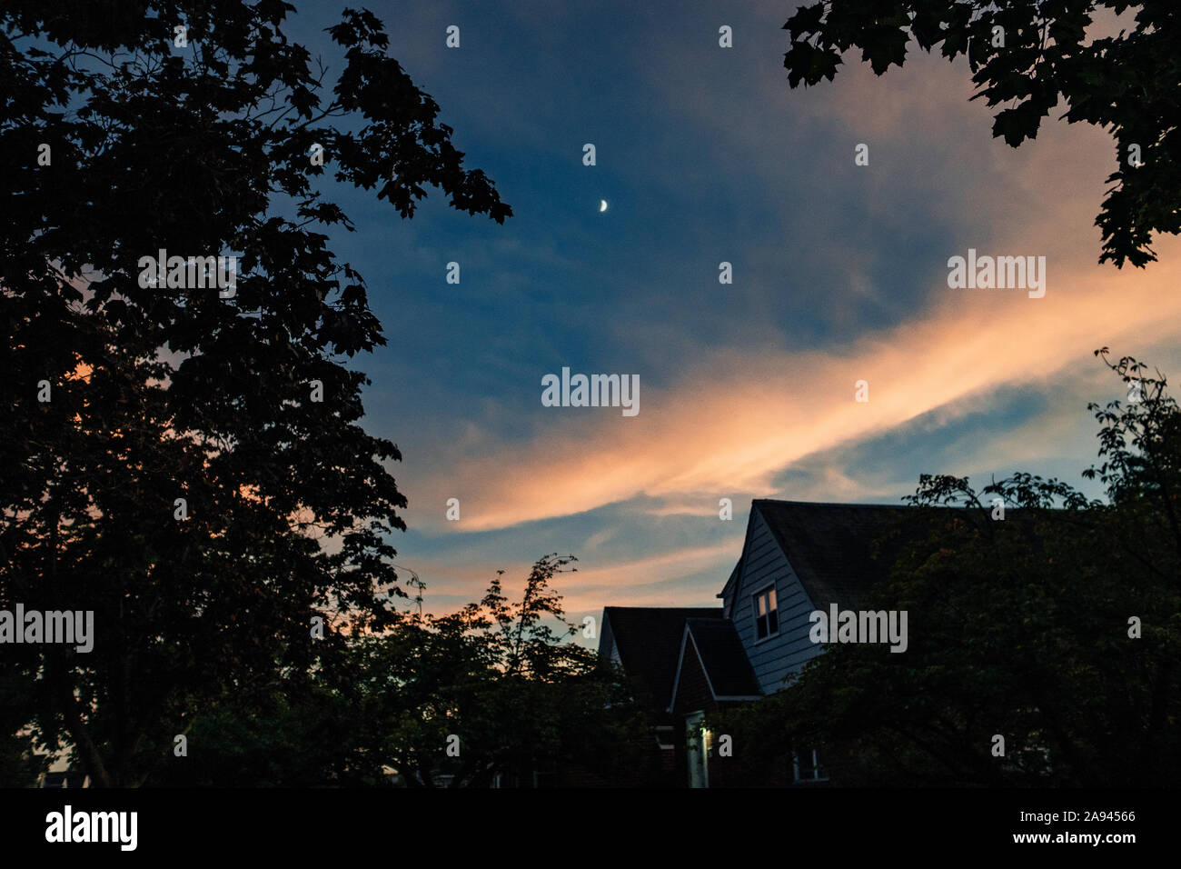 The moon appears in the sky over a neighborhood at sunset Stock Photo ...