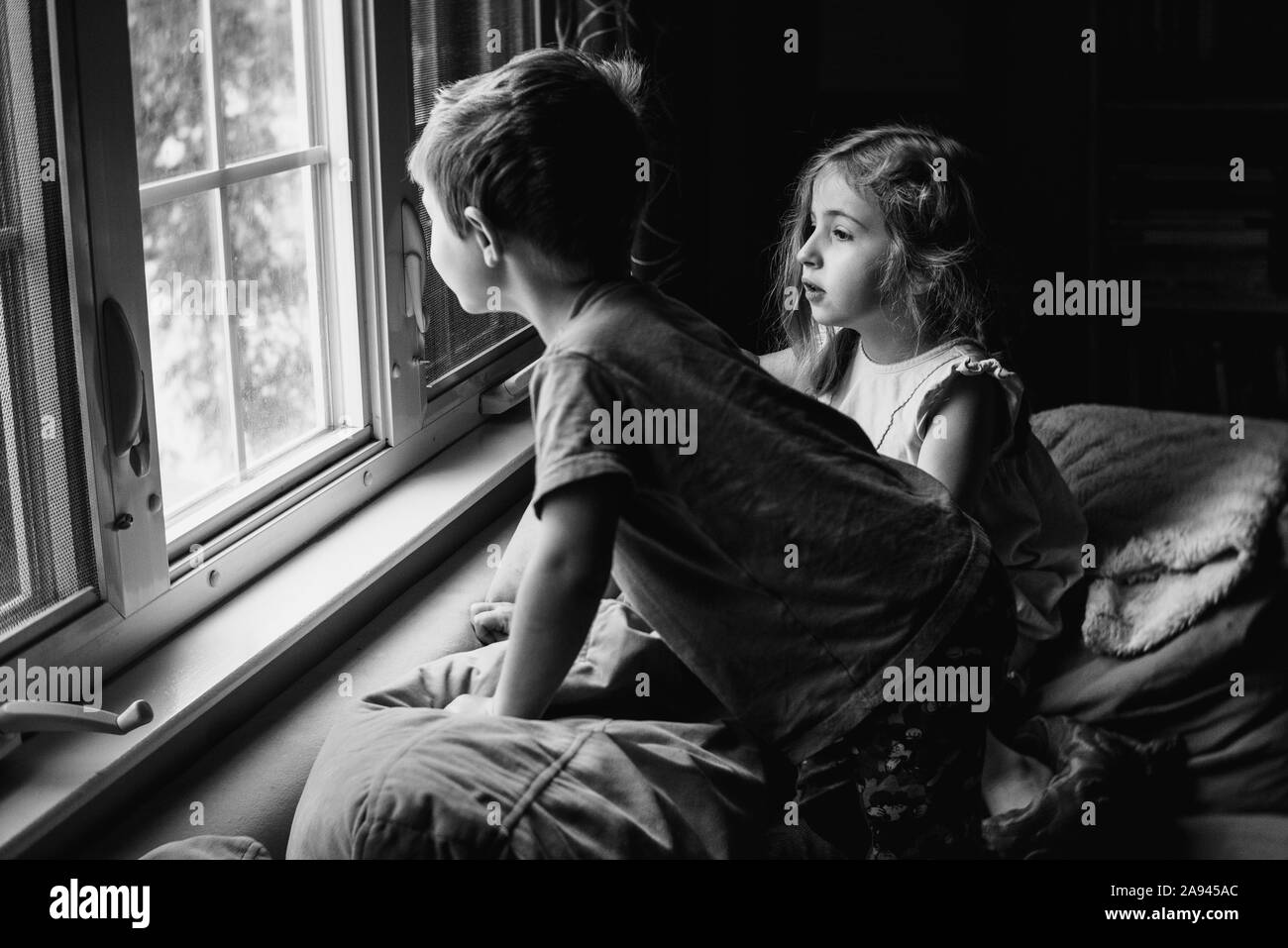 Two children perch on a couch and look out a window Stock Photo - Alamy