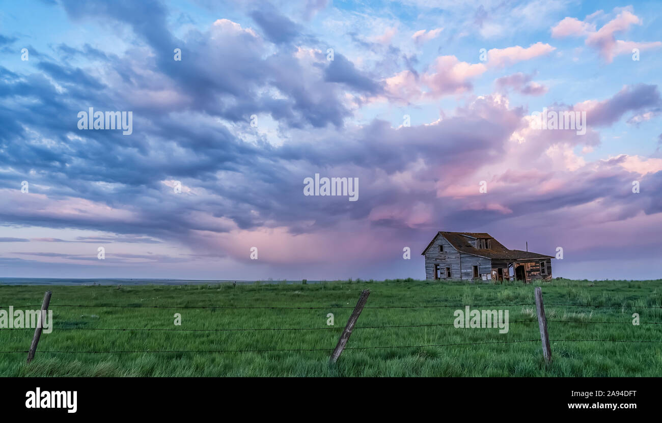 Old farmstead on the prairies under glowing storm clouds at sunset; Val ...