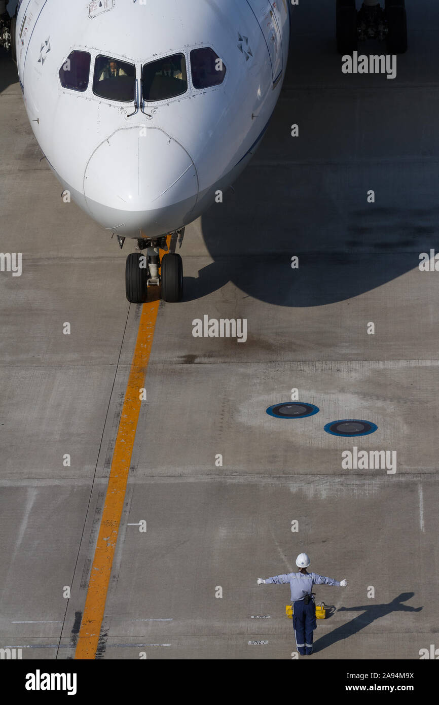A member of the ground crew directs an airliner on the apron at Haneda ...