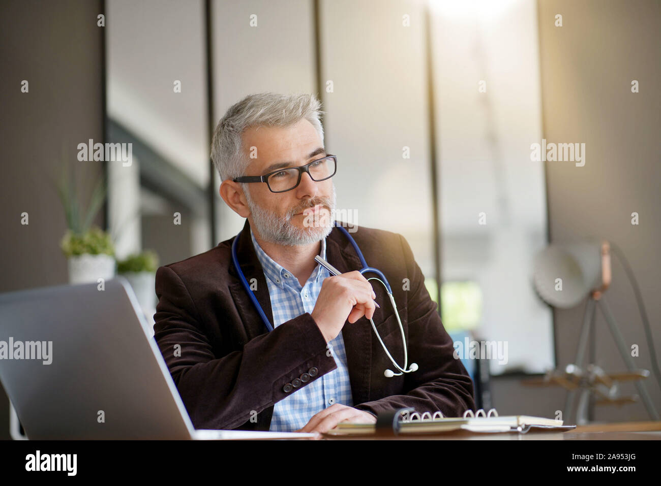 General practitioner sitting at his desk in medical office Stock Photo ...